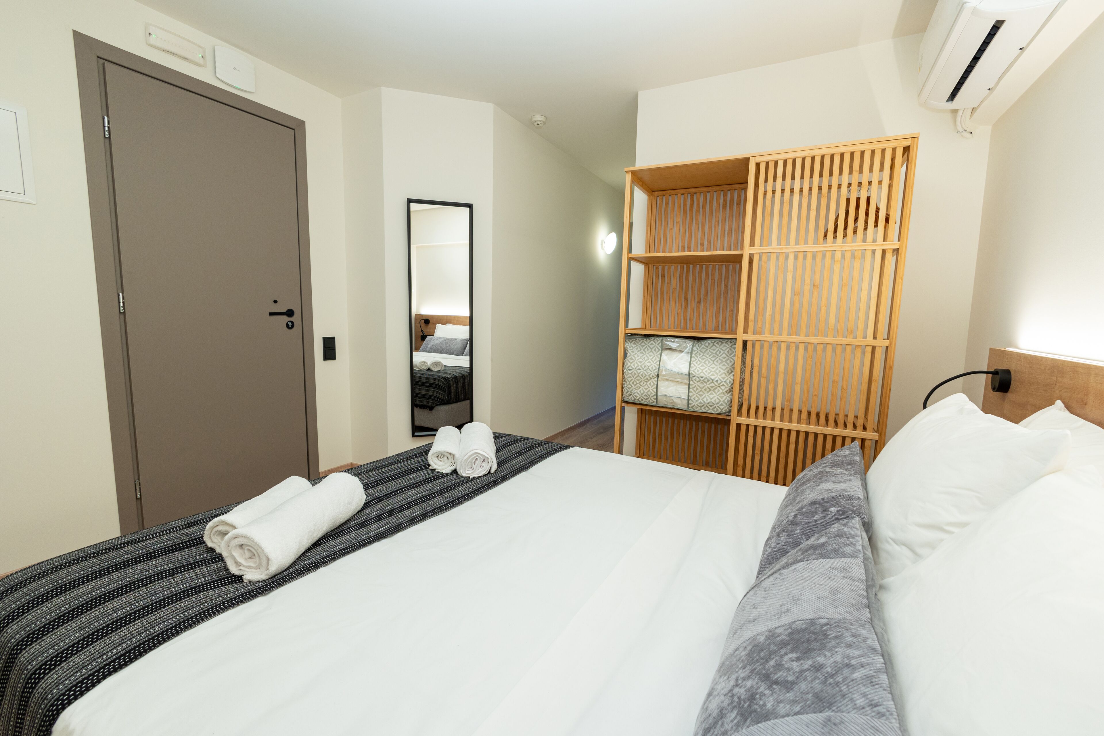 Quarto de hotel com cama, guarda-roupa, espelho e ar condicionado.