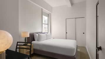 Quarto de hotel moderno com uma cama, uma escrivaninha com luminária, uma janela e uma porta.