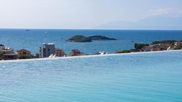 Piscina com vista para o mar e edifícios ao fundo.