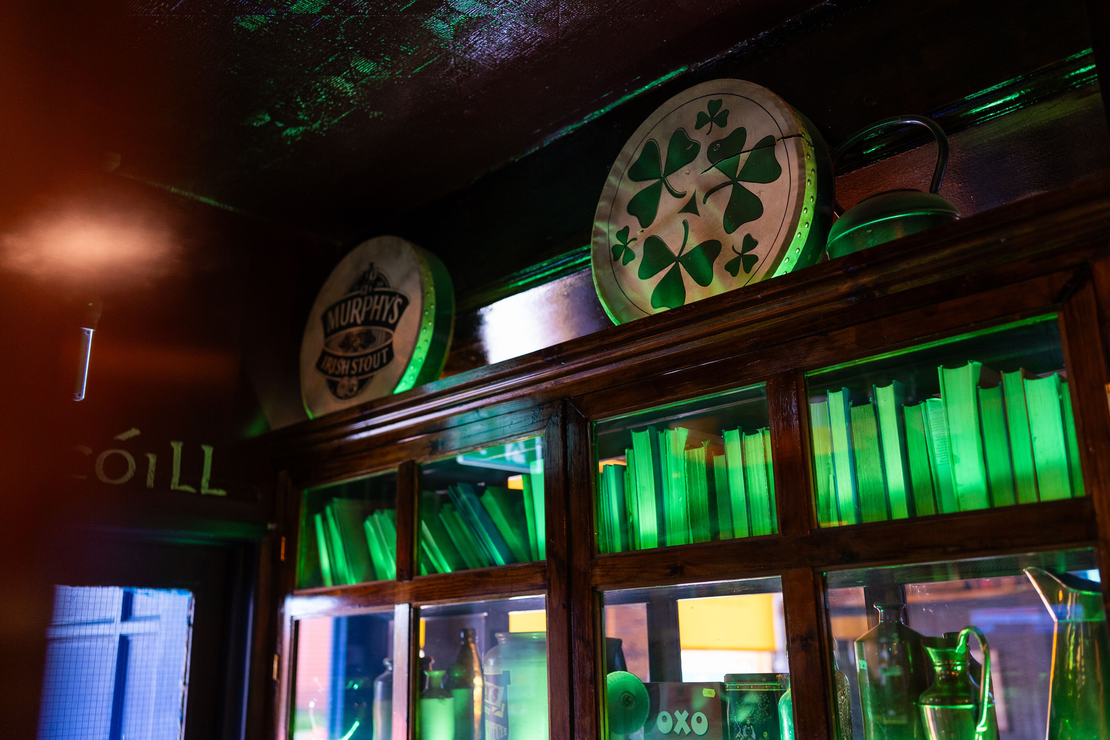 Um bar com iluminação verde e uma placa com a inscrição 'Murphy's Irish Stout'.