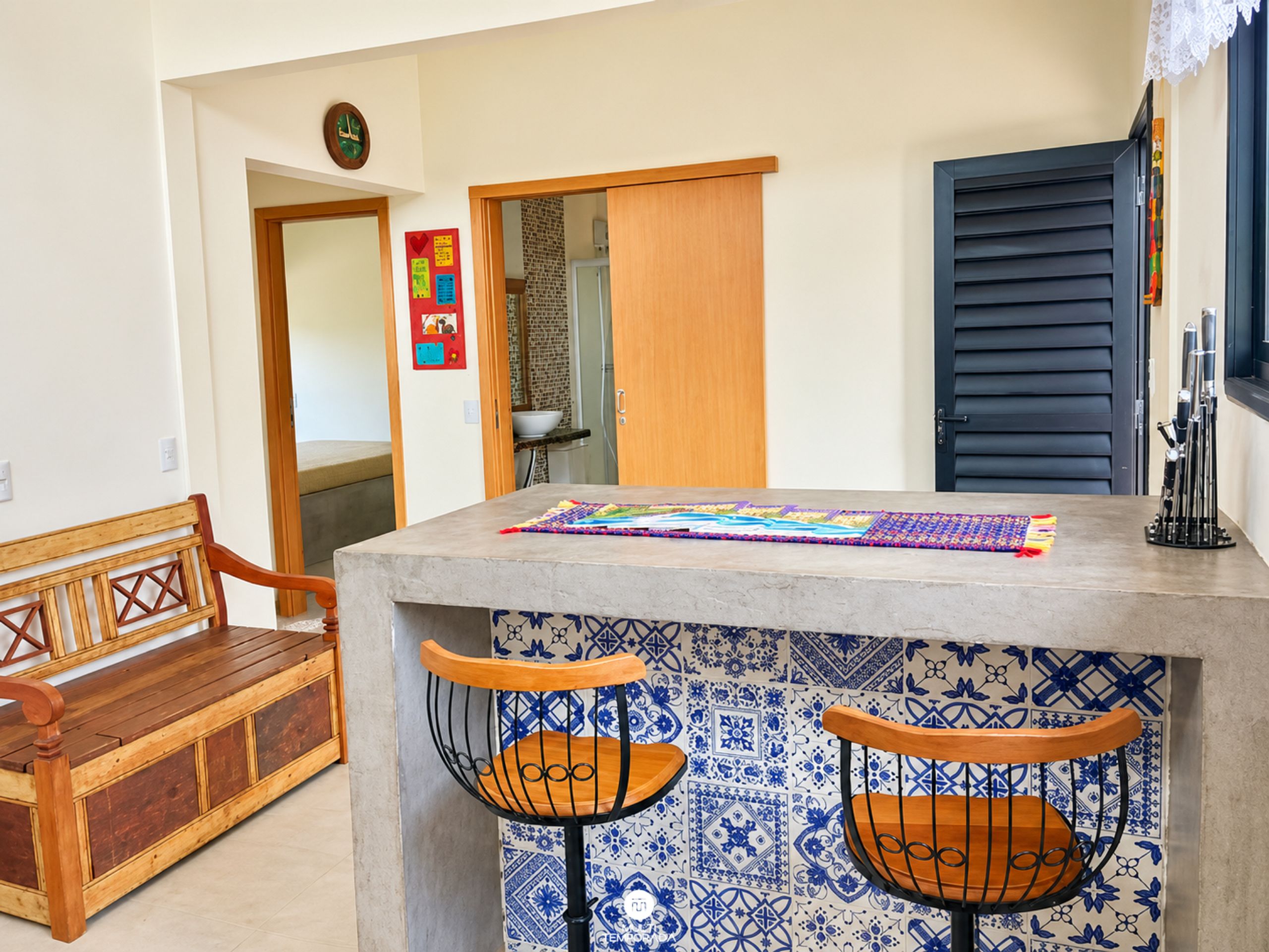 Uma cozinha com um banco de madeira, dois banquetas de bar, uma parede de azulejos e uma porta de madeira.