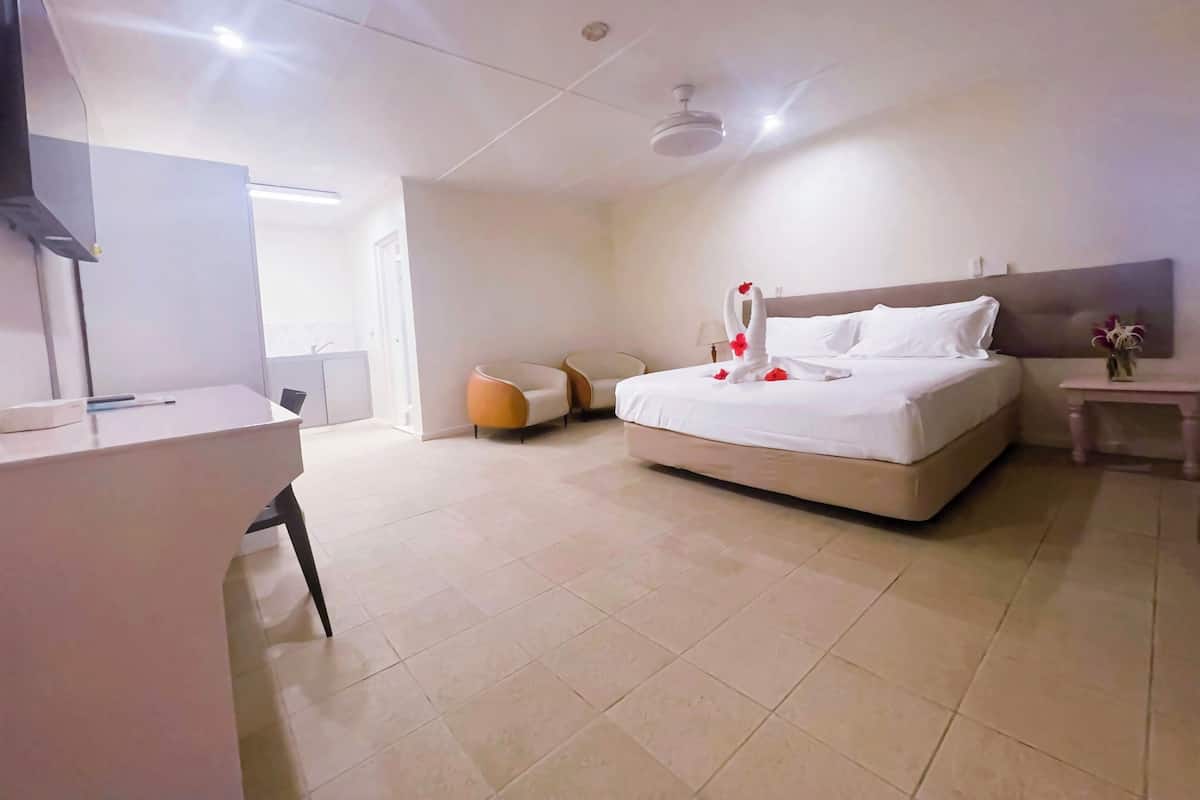 Quarto de hotel com cama, escrivaninha, cadeira, mesa de cabeceira e televisão na parede.