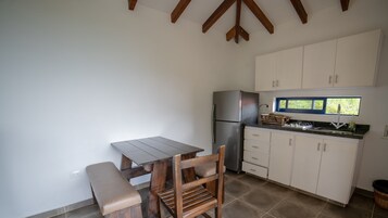 Uma cozinha compacta com mesa e banco de madeira, geladeira de aço inoxidável e armários brancos.