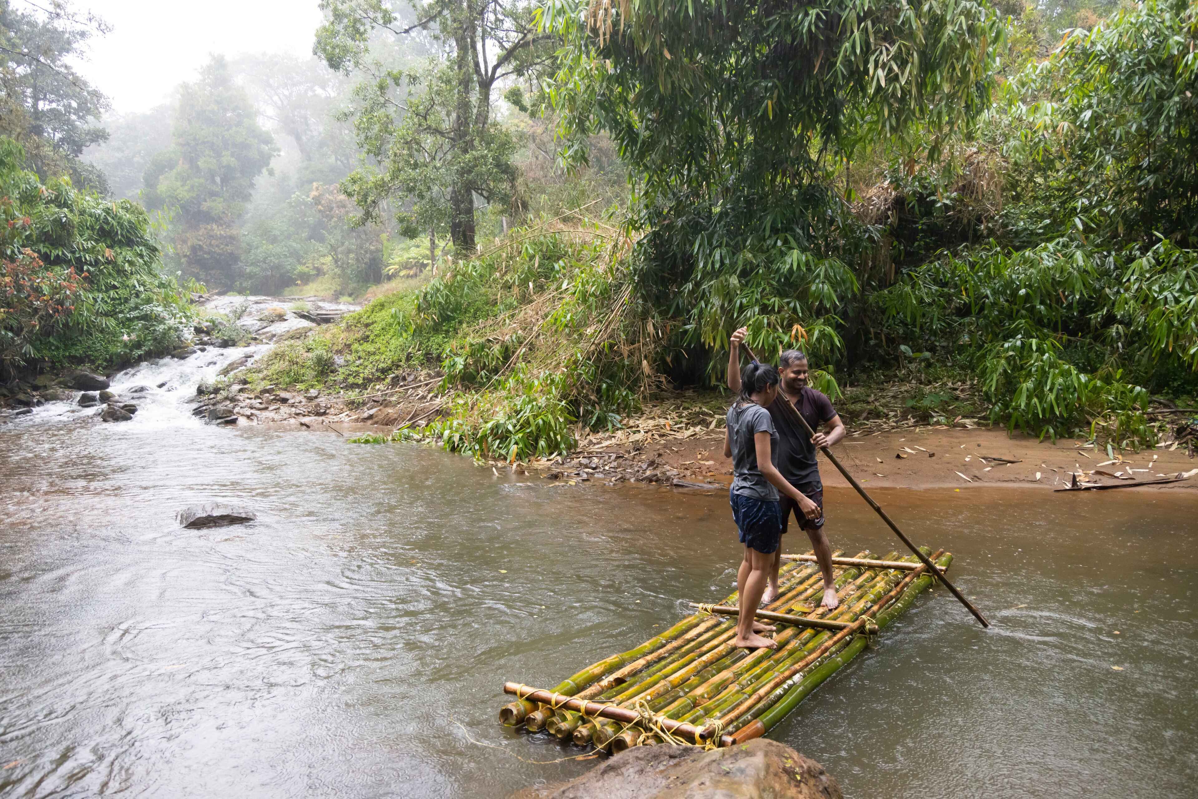 Duas pessoas em uma jangada de bambu em um rio, cercadas por vegetação densa.