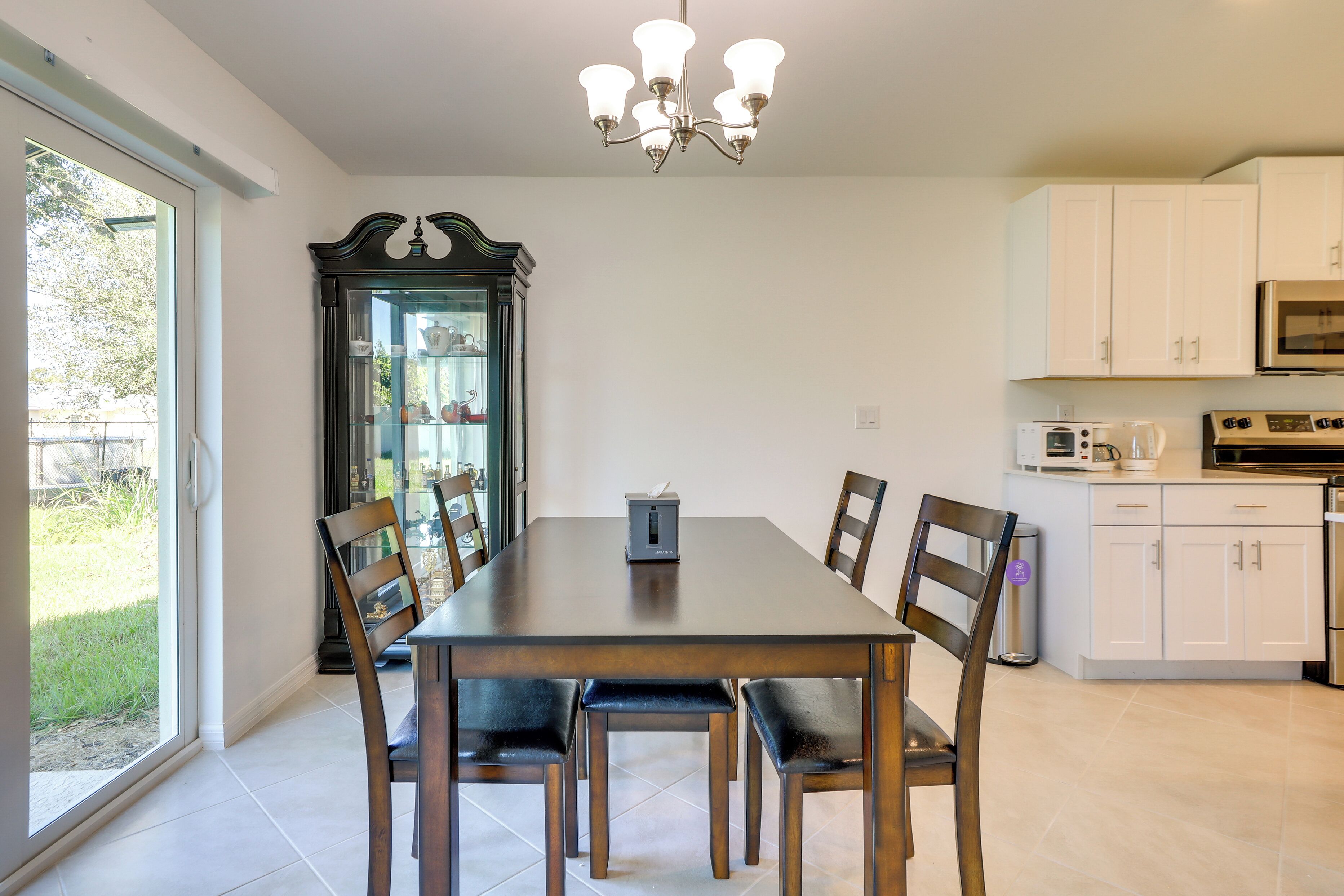 Uma sala de jantar com uma mesa e cadeiras de madeira, um candelabro e vista para o exterior através de uma porta de vidro.