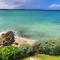 Vista costeira com águas azul-turquesa cristalinas, um litoral rochoso e vegetação exuberante.