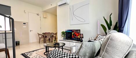 Uma sala de estar moderna com um sofá, uma mesa de centro e uma televisão. Há uma área de jantar com cadeiras e uma mesa.
