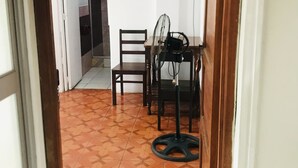 Um quarto com piso estampado, uma mesa de jantar com cadeiras, um ventilador e um abajur.