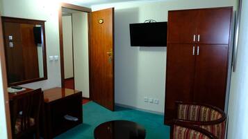 Quarto de hotel com armário de madeira, escrivaninha com espelho, televisão na parede e cadeira estampada.