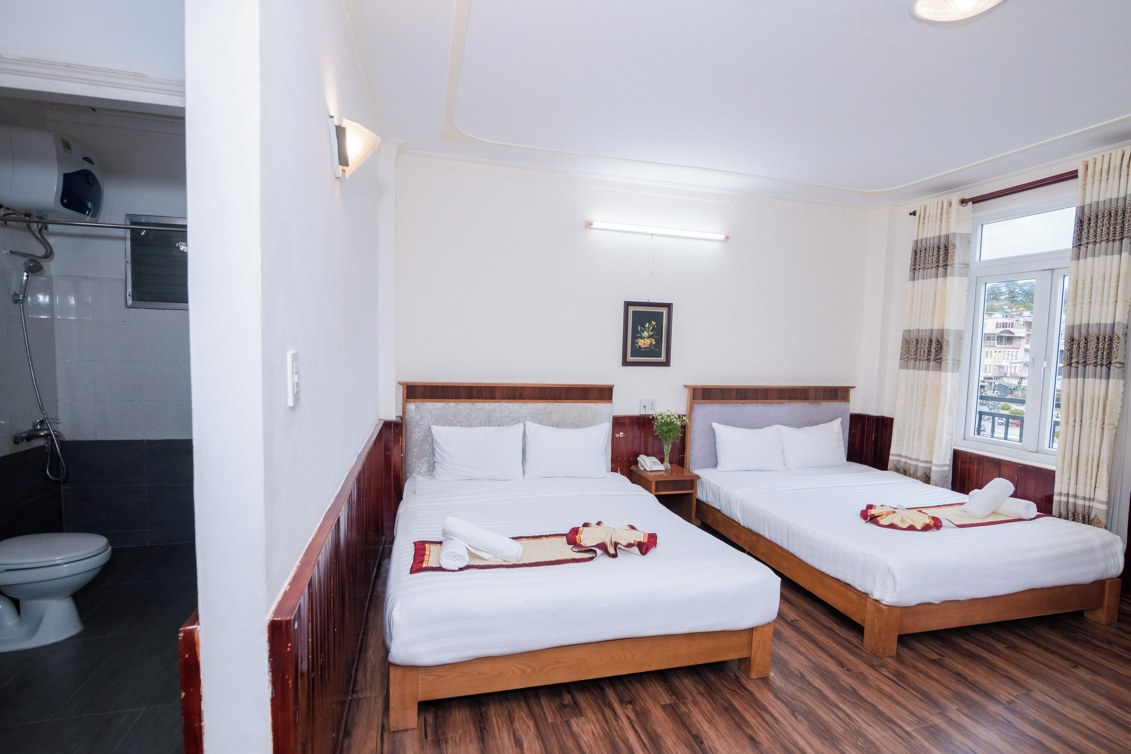 Quarto de hotel com duas camas, banheiro e janela com cortinas.