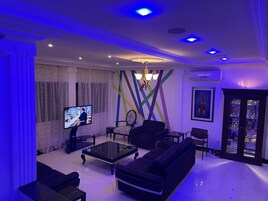 Uma sala de estar moderna com televisão de tela plana, sofás pretos, uma mesa de centro e um lustre.