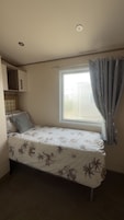Quarto com uma cama de solteiro, janela com persianas, cortina e armário embutido.
