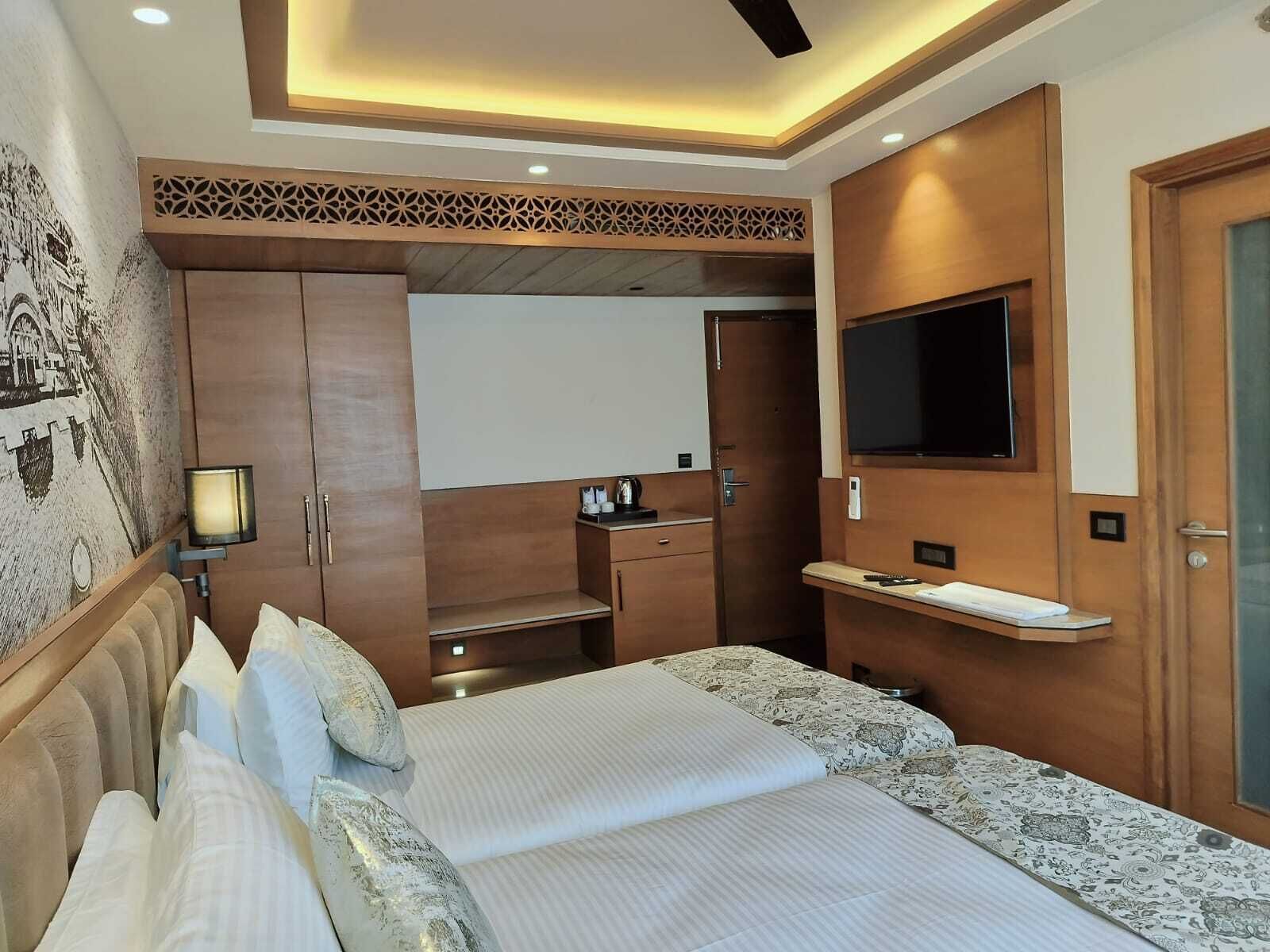 Quarto de hotel com uma cama, televisão na parede, escrivaninha com cadeira e guarda-roupa.
