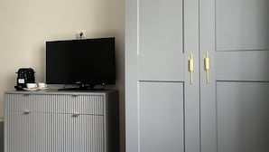 Quarto com um guarda-roupa cinzento, uma televisão sobre um móvel e uma máquina de café.