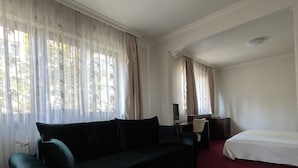 Quarto com um sofá de cor escura, uma cama, uma televisão e um abajur.