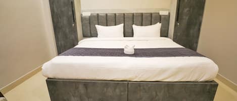 Cama bem arrumada com edredom branco e almofadas, cabeceira cinza e estrutura de cama cinza.