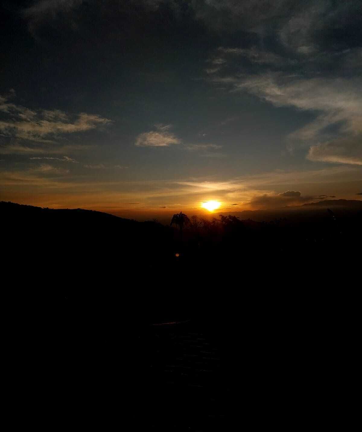 Um pôr do sol sobre uma paisagem acidentada, com a silhueta de uma pessoa ao longe.
