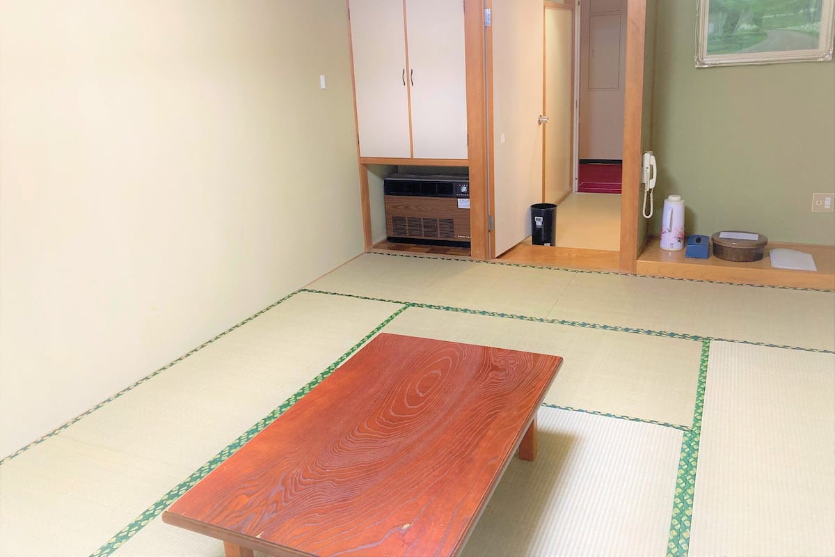 Quarto com tatame, uma mesa de madeira, guarda-roupa, aquecedor e telefone.