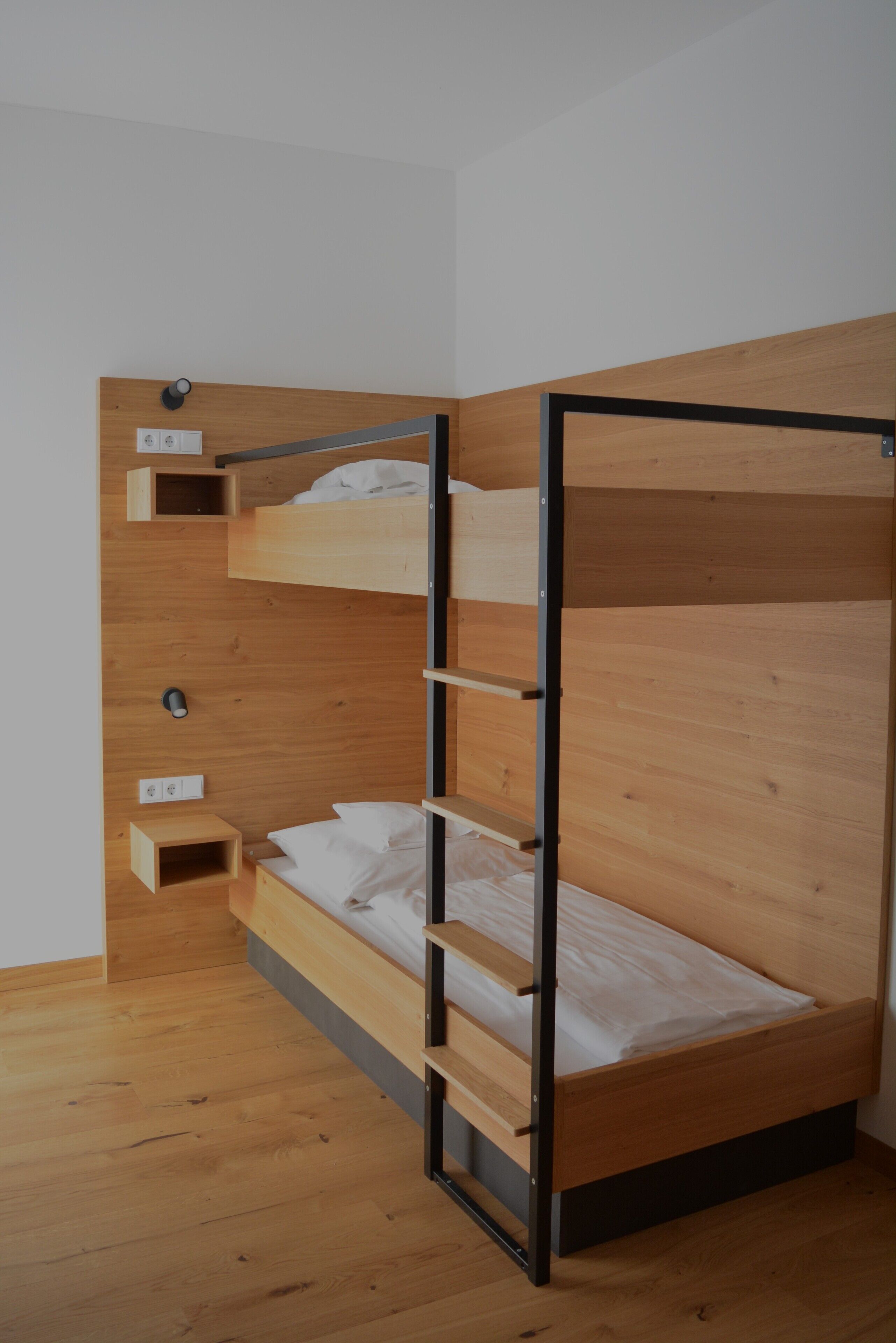 Uma cama de solteiro com cabeceira e peseira de madeira, compartimentos de armazenamento embutidos e uma pequena mesa de cabeceira.