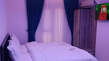 Quarto com cama, mesas de cabeceira, televisão e guarda-roupa de madeira.