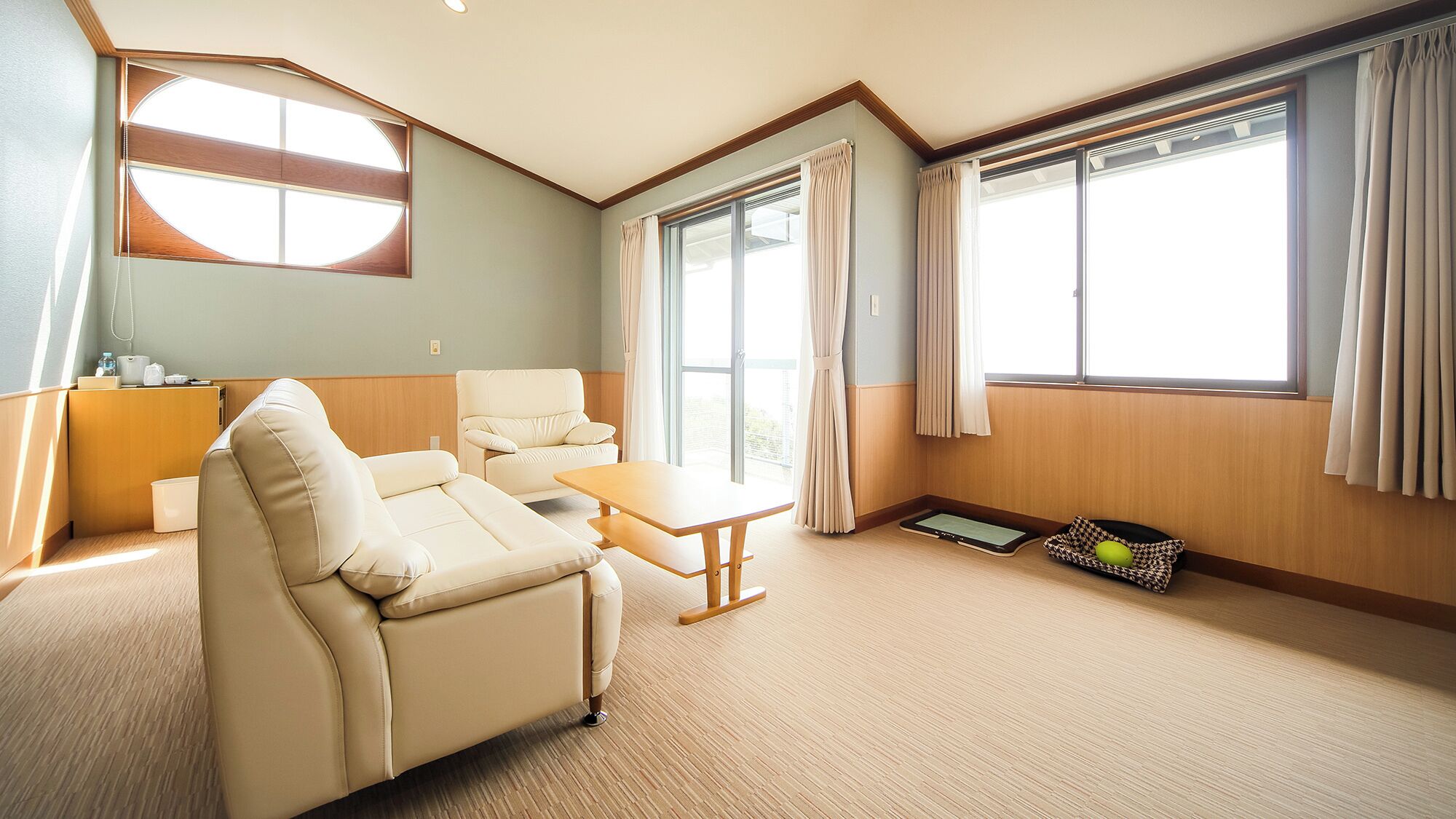Quarto com sofá, uma pequena mesa, armário de madeira e grandes janelas com cortinas.