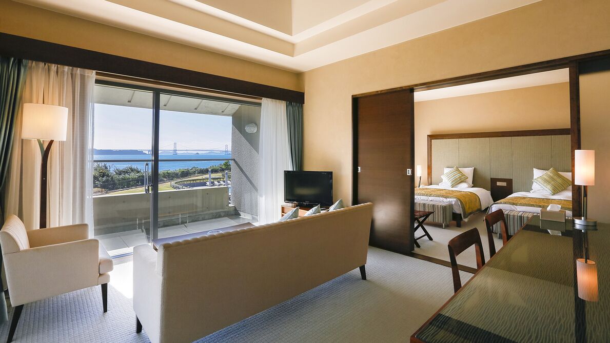 Quarto de hotel com varanda, televisão, sofá, mesa de jantar e uma cama.