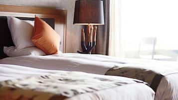 Quarto de hotel com duas camas, uma mesa de cabeceira com abajur e uma cadeira.