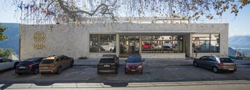 Um hotel com fachada moderna, um estacionamento com vários carros e vista para as montanhas ao fundo.