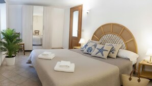 Quarto de hotel com uma cama grande, uma planta em vaso, uma cabeceira de madeira e uma cesta de palha.