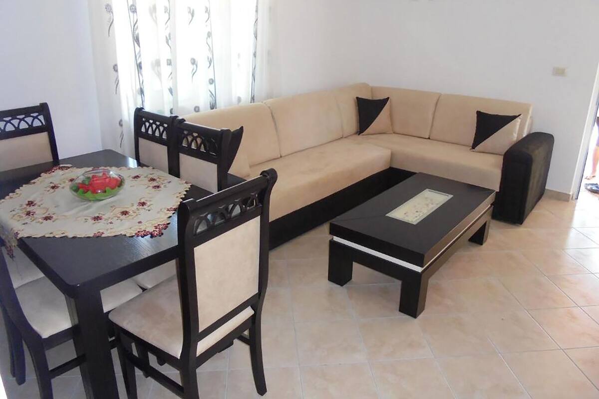 Uma sala de estar com um sofá bege, uma mesa de centro e uma mesa de jantar com cadeiras.