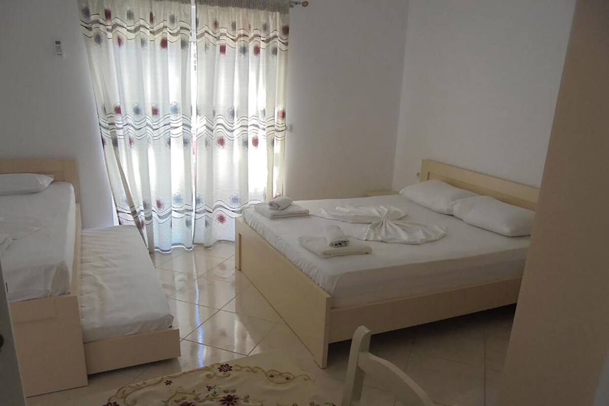 Quarto de hotel com uma cama de casal, uma cama individual e uma cadeira.