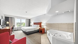 Quarto de hotel com cama, escrivaninha com cadeira, poltrona vermelha, janela grande e banheira.