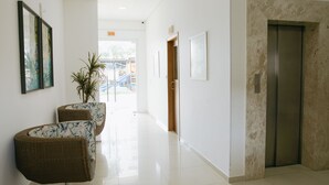 Um hall de entrada limpo e moderno, com cadeiras de vime, uma planta em vaso e um elevador de mármore.