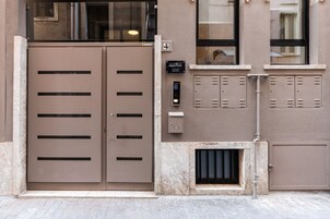Fachada de edifício com uma grande porta dupla, um teclado numérico e várias caixas de serviços.