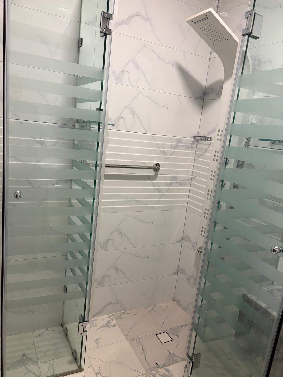Box de chuveiro envidraçado com piso de mármore e chuveiro.