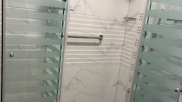 Box de chuveiro envidraçado com piso de mármore e chuveiro.