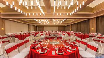 Salão de banquetes com mesas redondas, cadeiras brancas e fitas vermelhas, e um lustre central.