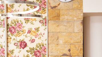 Uma área de recepção com papel de parede floral, um relógio e um vaso com tulipas.