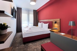 Quarto de hotel moderno com cama, mesa de cabeceira, luminária e planta em vaso.