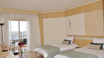 Quarto de hotel com duas camas, varanda com vista, área de jantar e uma pequena mesa com um vaso de flores.