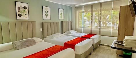 Quarto de hotel com três camas, uma janela grande e obras de arte na parede.