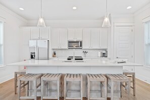 Uma cozinha moderna com armários brancos, eletrodomésticos de aço inoxidável e banquetas de madeira.