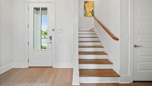 Um interior limpo e claro, com escada de madeira e porta com painel de vidro jateado.