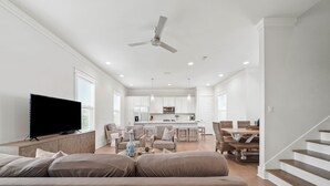 Uma sala de estar moderna com uma televisão de tela plana grande, um sofá bege e uma área de jantar com uma mesa e cadeiras de madeira.