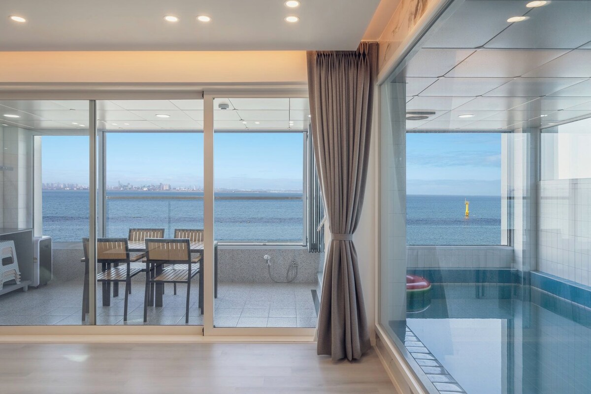 Quarto com uma grande porta de correr de vidro que dá para uma varanda com vista para o mar e o horizonte da cidade.