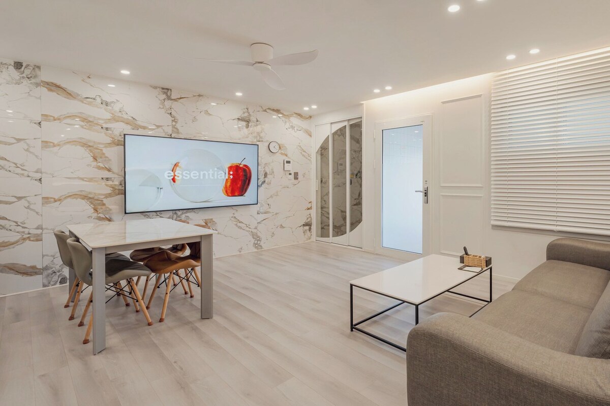 Uma sala de estar moderna com parede de mármore, televisão de tela plana, área de jantar com cadeiras, sofá e mesa de centro.