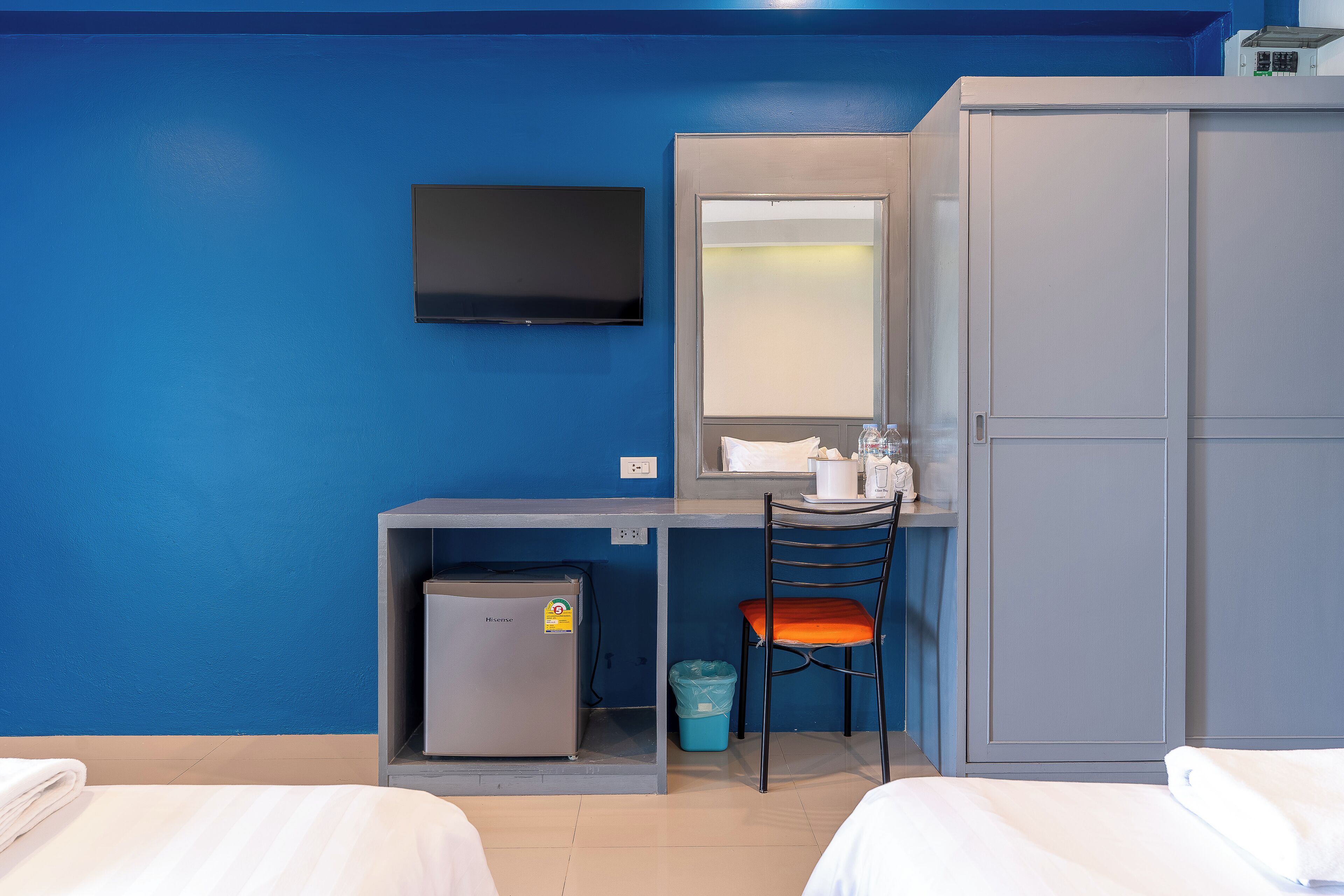 Quarto de hotel com cama, escrivaninha com computador, televisão, guarda-roupa e lixeira.