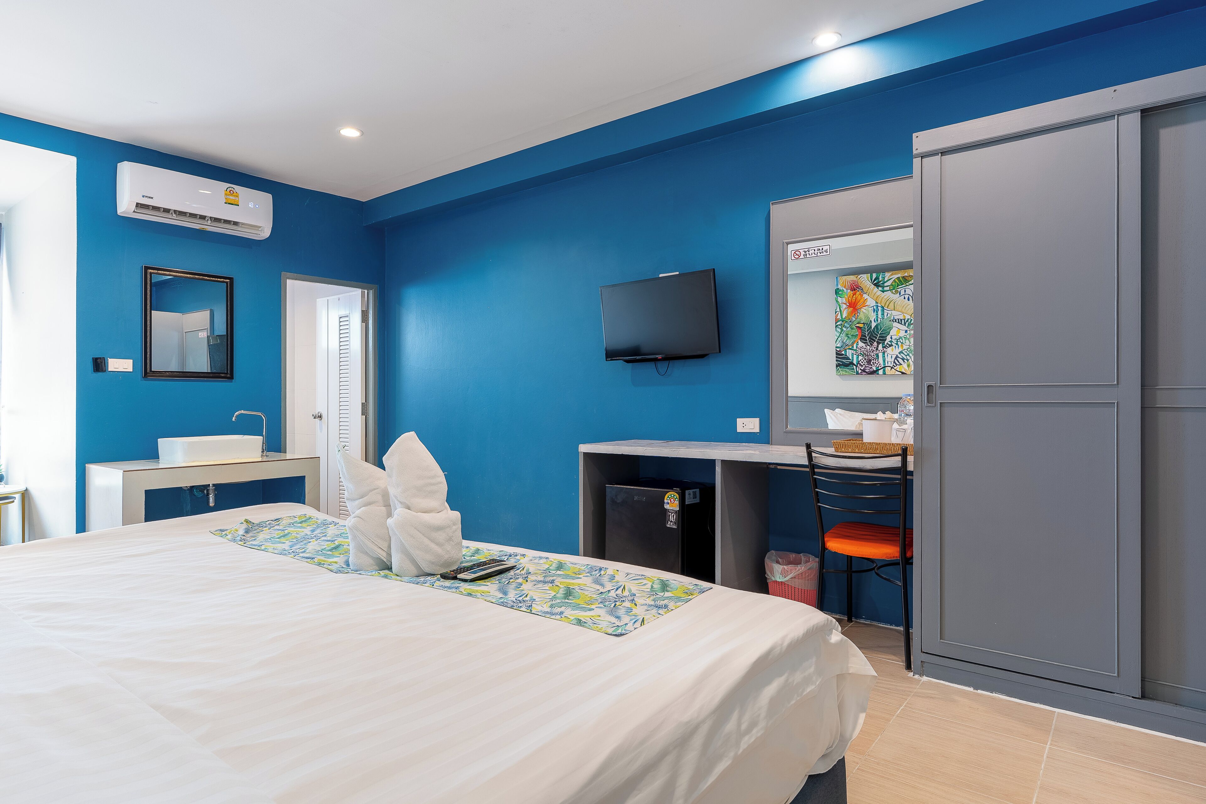 Quarto de hotel com cama, escrivaninha, cadeira, televisão e guarda-roupa.