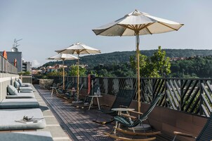 Terraço no telhado com área de estar externa, guarda-s óis e vista para uma paisagem montanhosa.