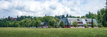 Um edifício moderno com um design de telhado singular, rodeado por um campo verde e árvores.